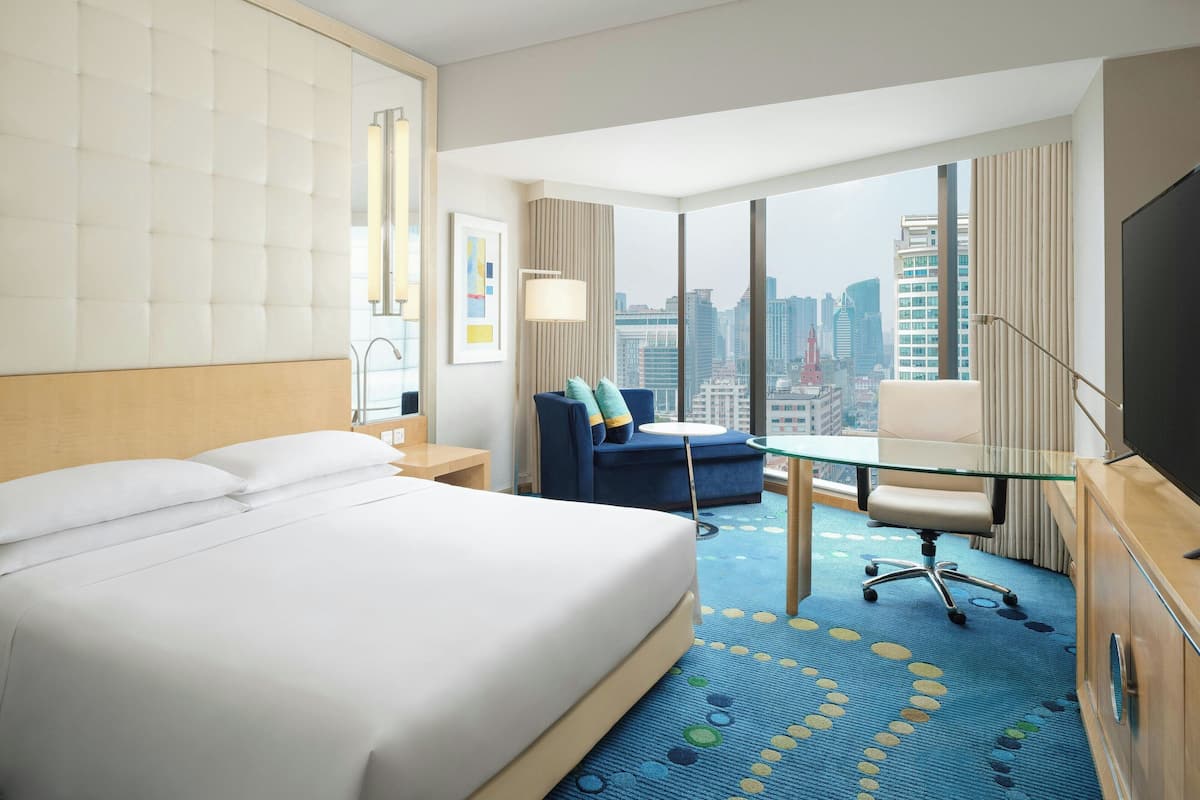 Quarto de hotel com uma cama grande, uma escrivaninha, uma cadeira e vista para a cidade.