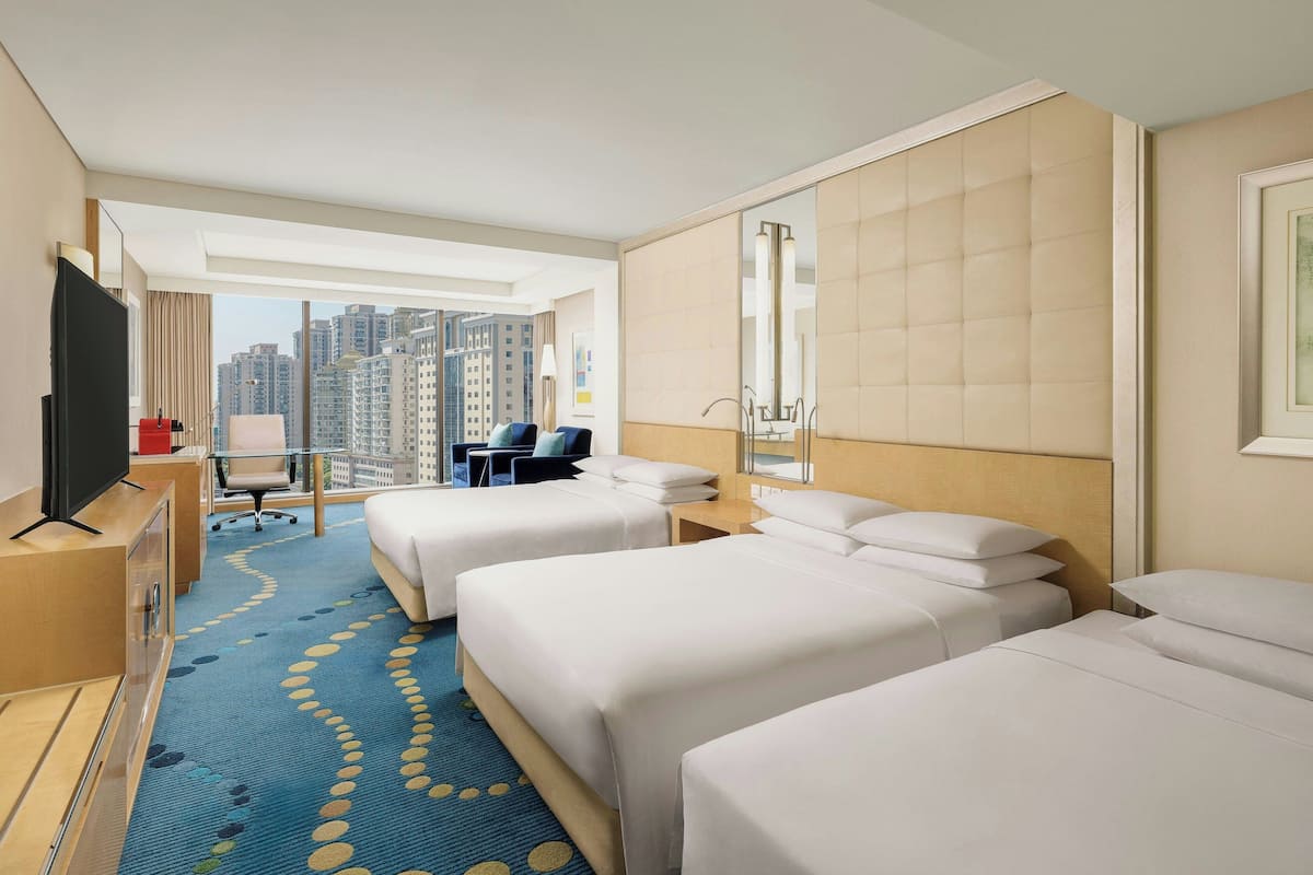 Quarto de hotel com duas camas, uma escrivaninha, uma cadeira e uma televisão.