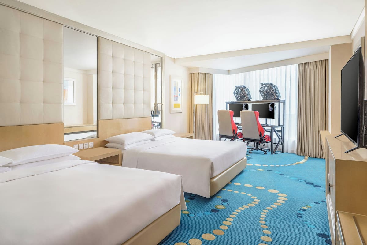 Quarto de hotel com duas camas, uma mesa de trabalho com cadeira, televisão e um espelho grande.