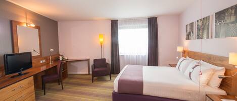 Quarto de hotel com cama, escrivaninha, cadeira, televisão e obras de arte nas paredes.