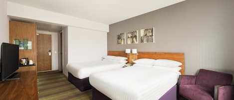 Quarto de hotel com duas camas, uma televisão, uma máquina de café e uma poltrona roxa.