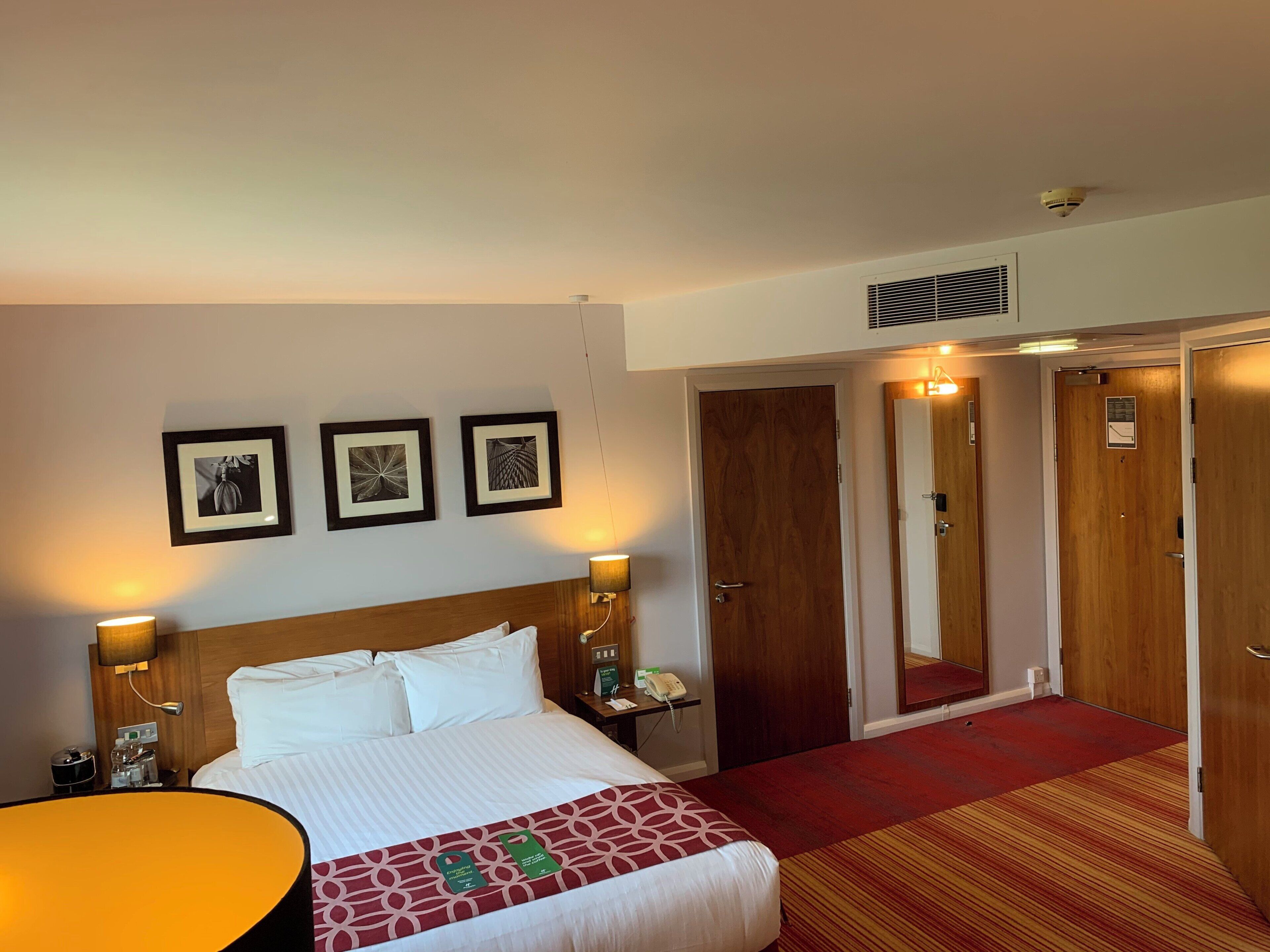 Quarto de hotel com cama, mesas de cabeceira, abajur, telefone e quadro na parede.