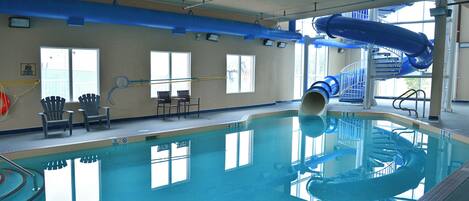 Piscina interna com escorregador, cadeiras e aviso de proibição de mergulho.