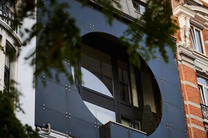 Fachada de edifício com uma grande janela circular, parte em tijolo e estrutura metálica.