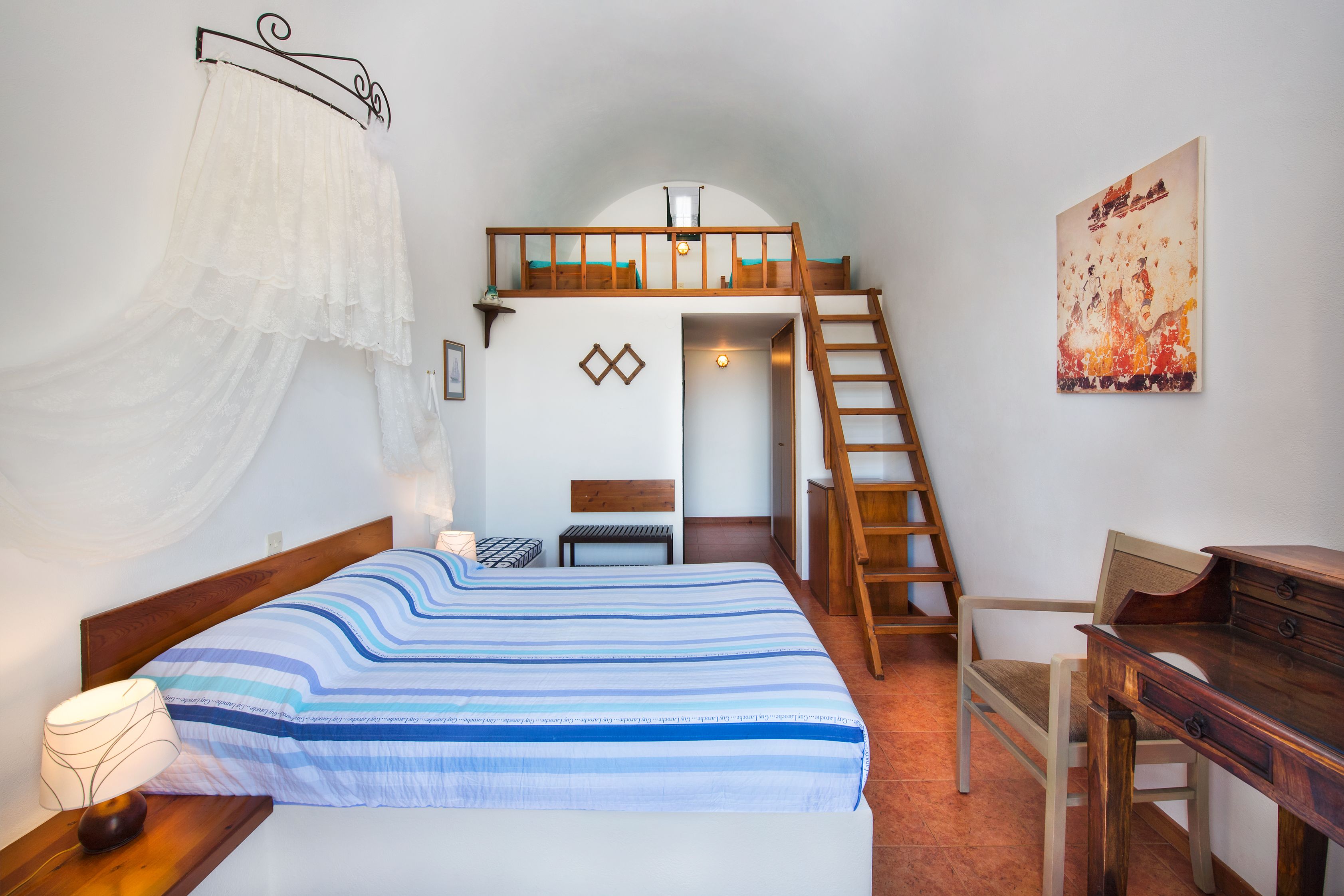 Quarto com cama, escrivaninha, cadeira, escada e varanda.