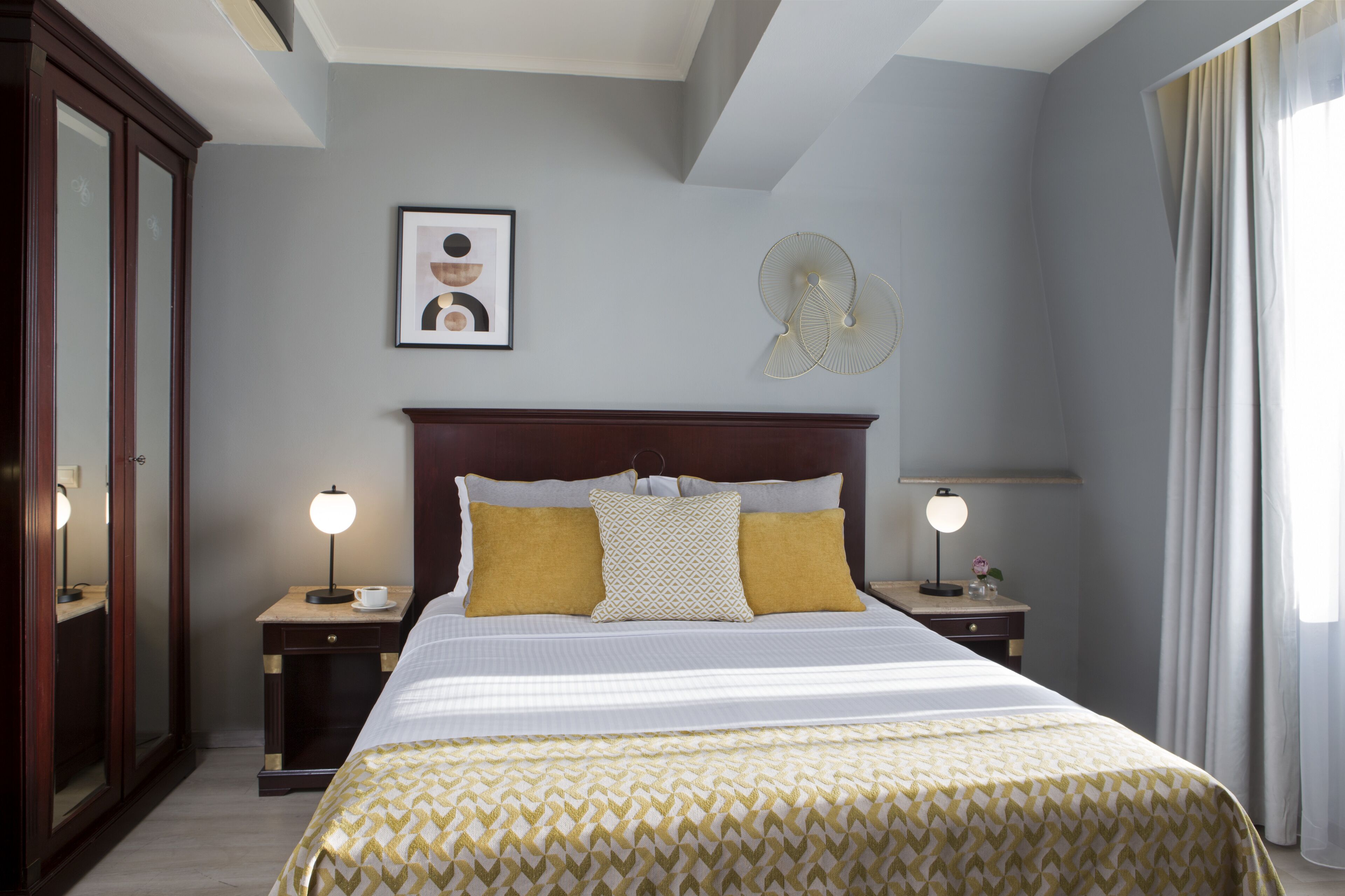 Quarto de hotel bem arrumado com uma cama grande, duas mesas de cabeceira com abajures, um ventilador fixado na parede e um quadro emoldurado sobre a cama.