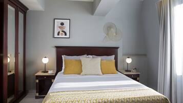 Quarto de hotel bem arrumado com uma cama grande, duas mesas de cabeceira com abajures, um ventilador fixado na parede e um quadro emoldurado sobre a cama.