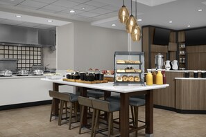 Cozinha moderna com ilha central, banquetas, espaço para café e TV na parede.