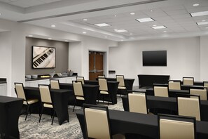 Sala de conferência com várias mesas e cadeiras, uma pintura grande na parede e uma porta que dá para outro espaço.