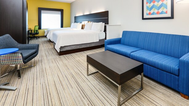Quarto de hotel com uma cama, um sofá azul, uma mesa de centro e uma escrivaninha com uma cadeira.