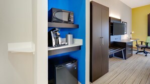 Quarto de hotel compacto com cozinha compacta, televisão de tela plana, escrivaninha e uma cadeira.