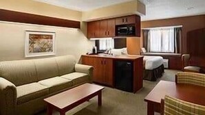 Quarto de hotel pequeno e funcional com sofá, mesa de jantar, kitchenette e cama.