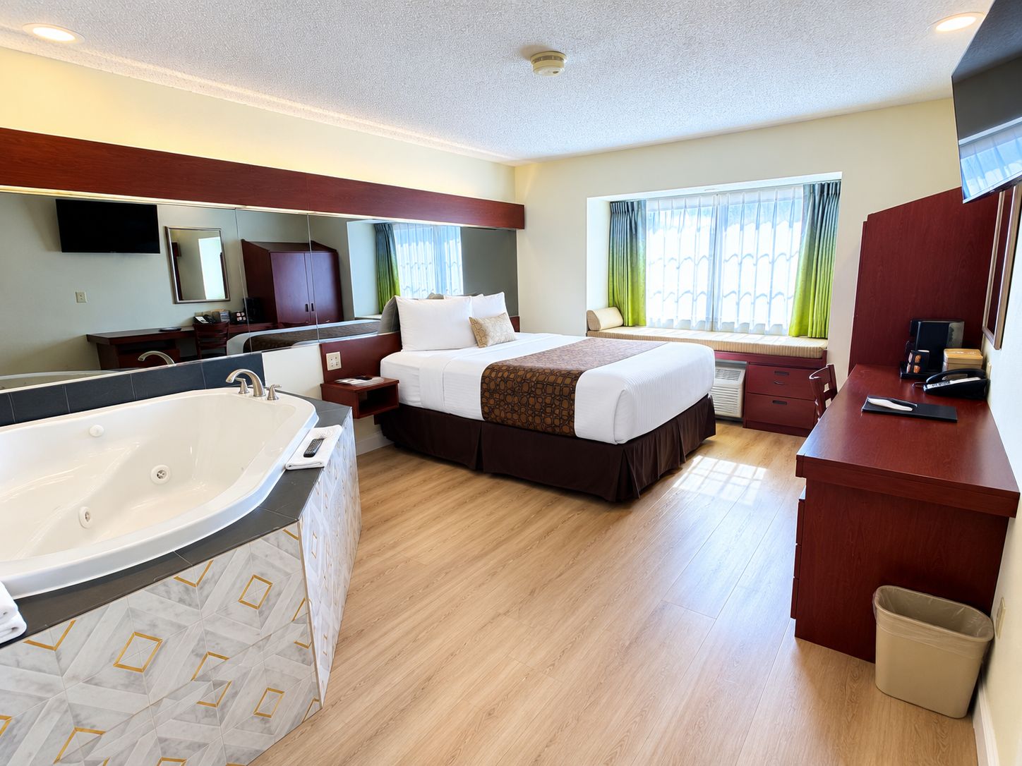 Quarto de hotel com cama grande, banheiro privativo com banheira, escrivaninha e janela com cortinas.
