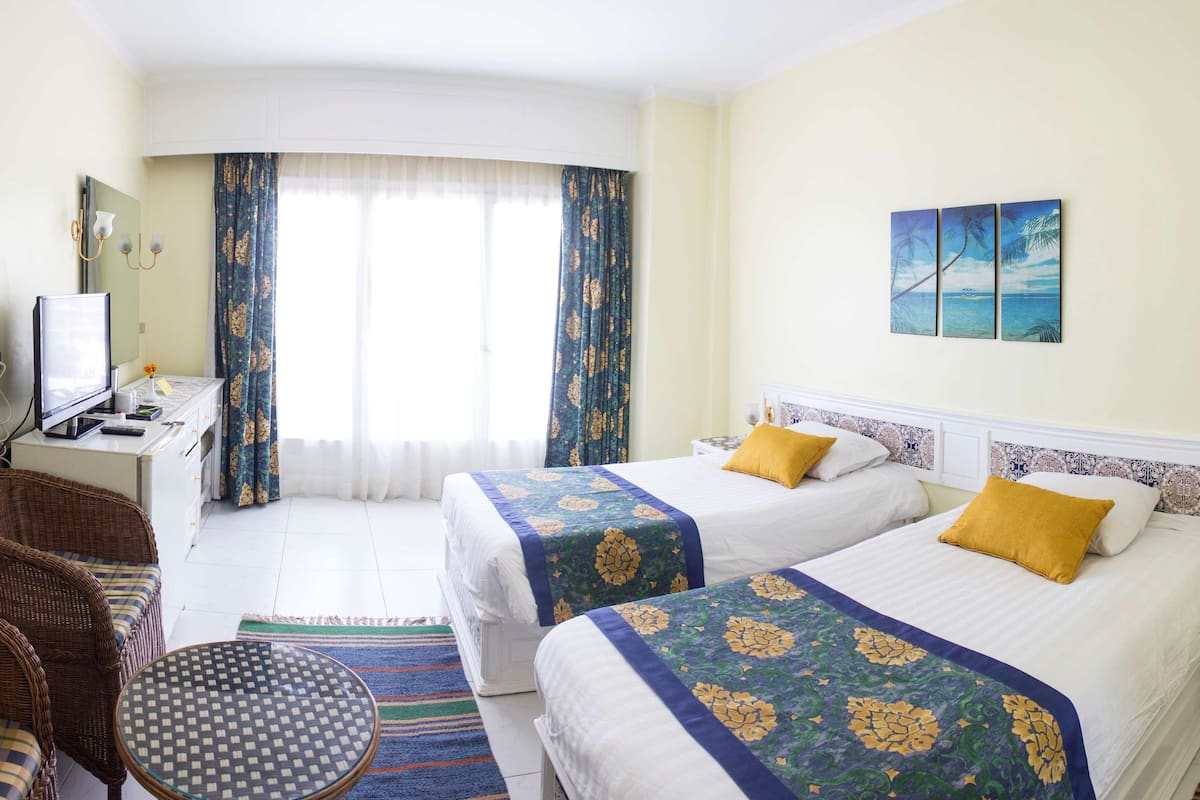 Quarto de hotel com duas camas, uma secretária com computador, uma cadeira e uma mesinha.