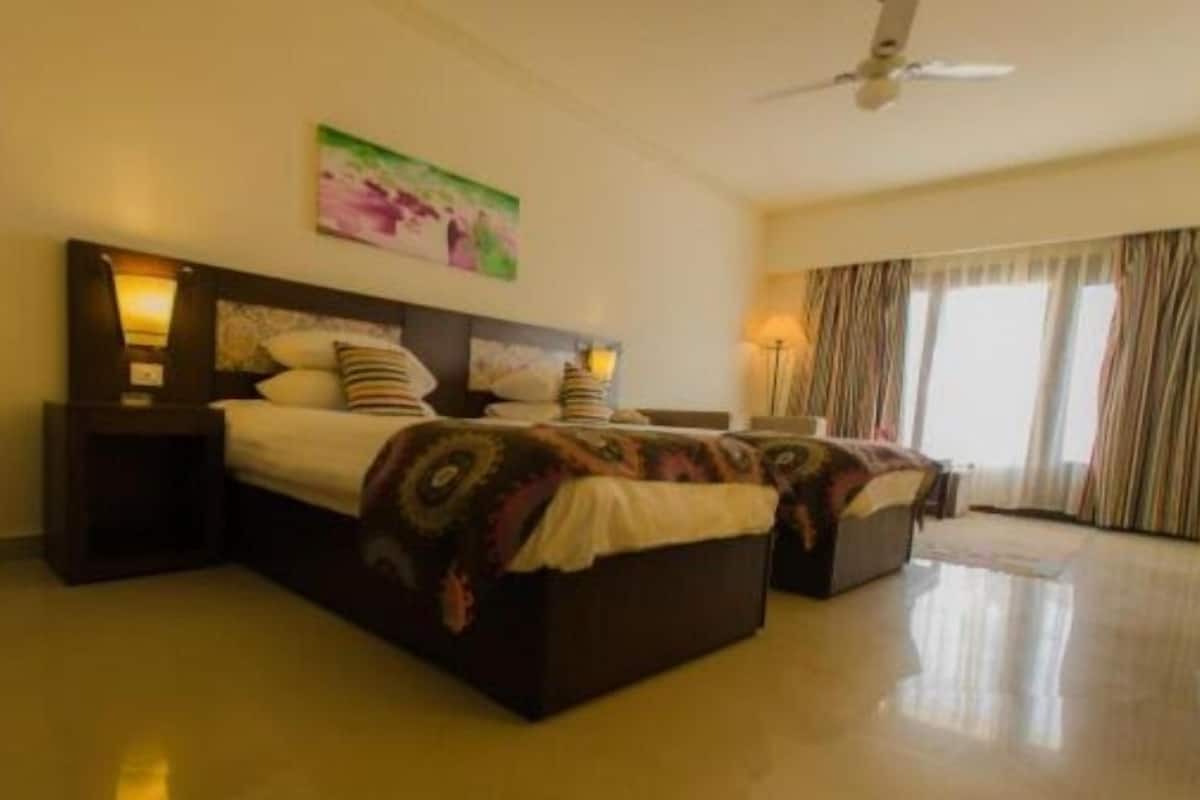 Quarto de hotel com uma cama grande, um ventilador de teto e um quadro na parede.