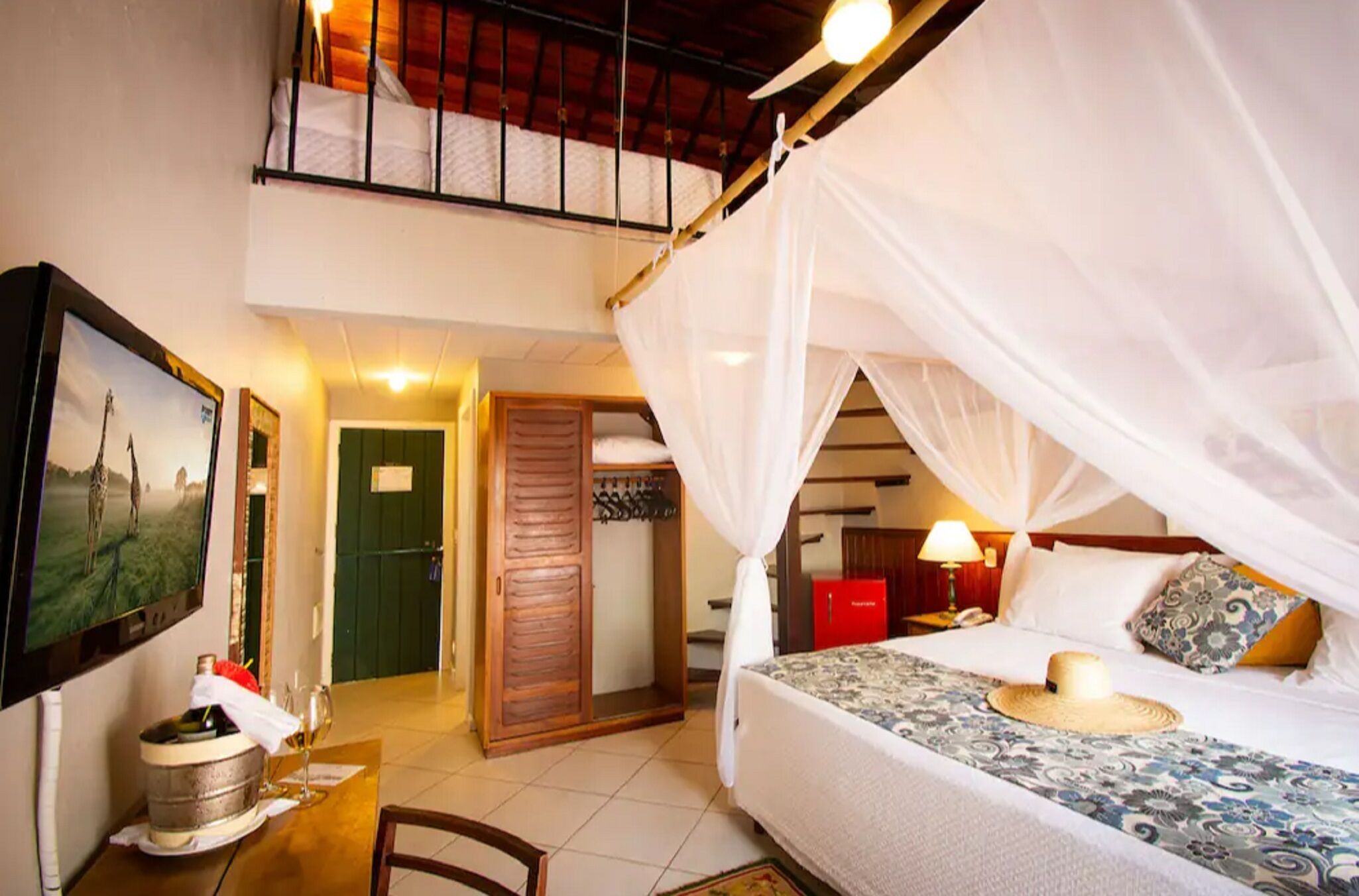 Quarto com cama, televisão, escrivaninha com cadeira, guarda-roupa e varanda com mosquiteiro.