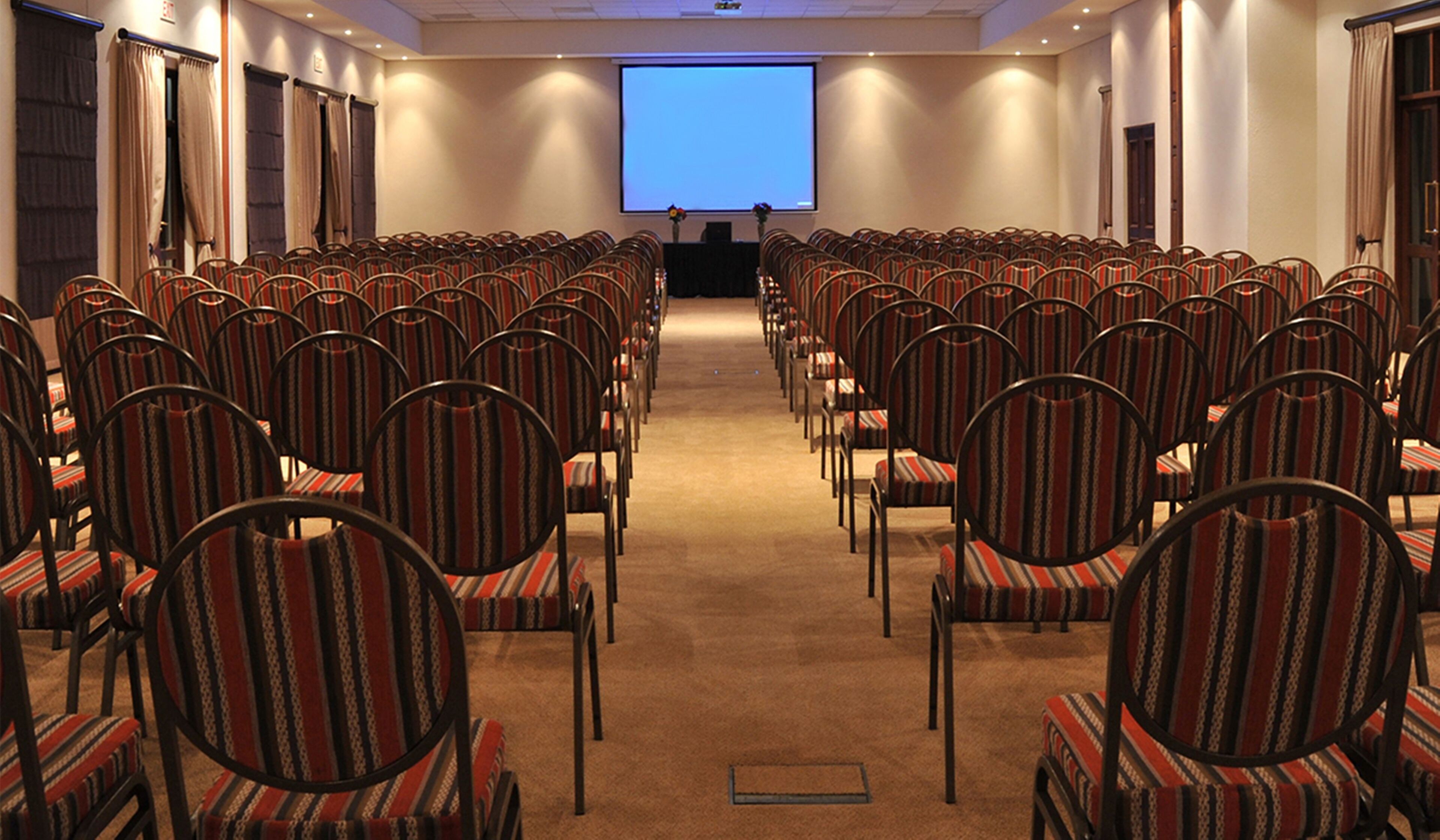 Uma sala de conferências com fileiras de cadeiras voltadas para uma tela grande na frente.