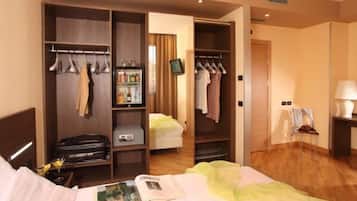 Quarto de hotel com cama, guarda-roupa com roupas penduradas, televisão e mesa de cabeceira.