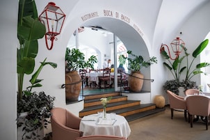 Uma área de refeições interna com um arco branco, plantas em vasos, mobiliário de vime e vista para a sala de jantar.