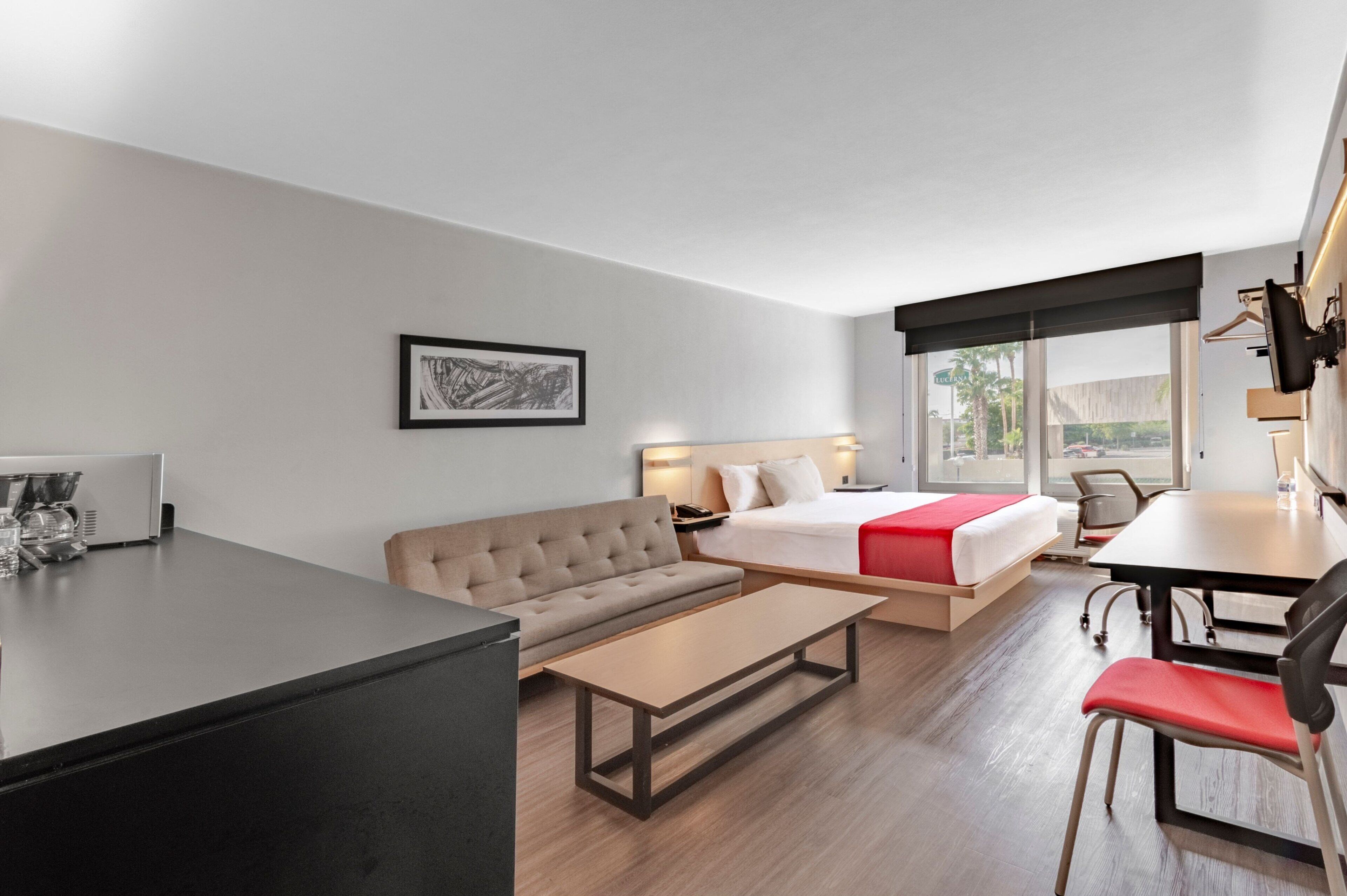 Quarto de hotel moderno com cama, sofá, mesa de jantar e máquina de café.