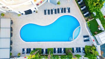 Vista aérea de uma piscina com espreguiçadeiras e guarda-sóis, cercada por vegetação e uma estrutura de edifício.