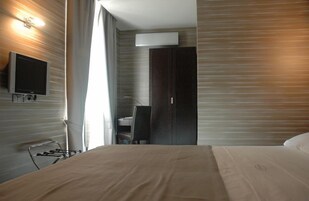Quarto de hotel com cama, escrivaninha, cadeira, televisão na parede e guarda-roupa.