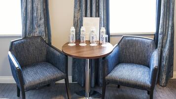 Quarto de hotel com cama, duas poltronas, mesa redonda pequena com artigos de higiene pessoal e janela com cortinas.