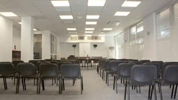 Uma sala de conferências com fileiras de cadeiras, uma mesa comprida e um quadro branco.