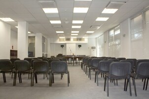 Uma sala de conferências com fileiras de cadeiras, uma mesa comprida e um quadro branco.
