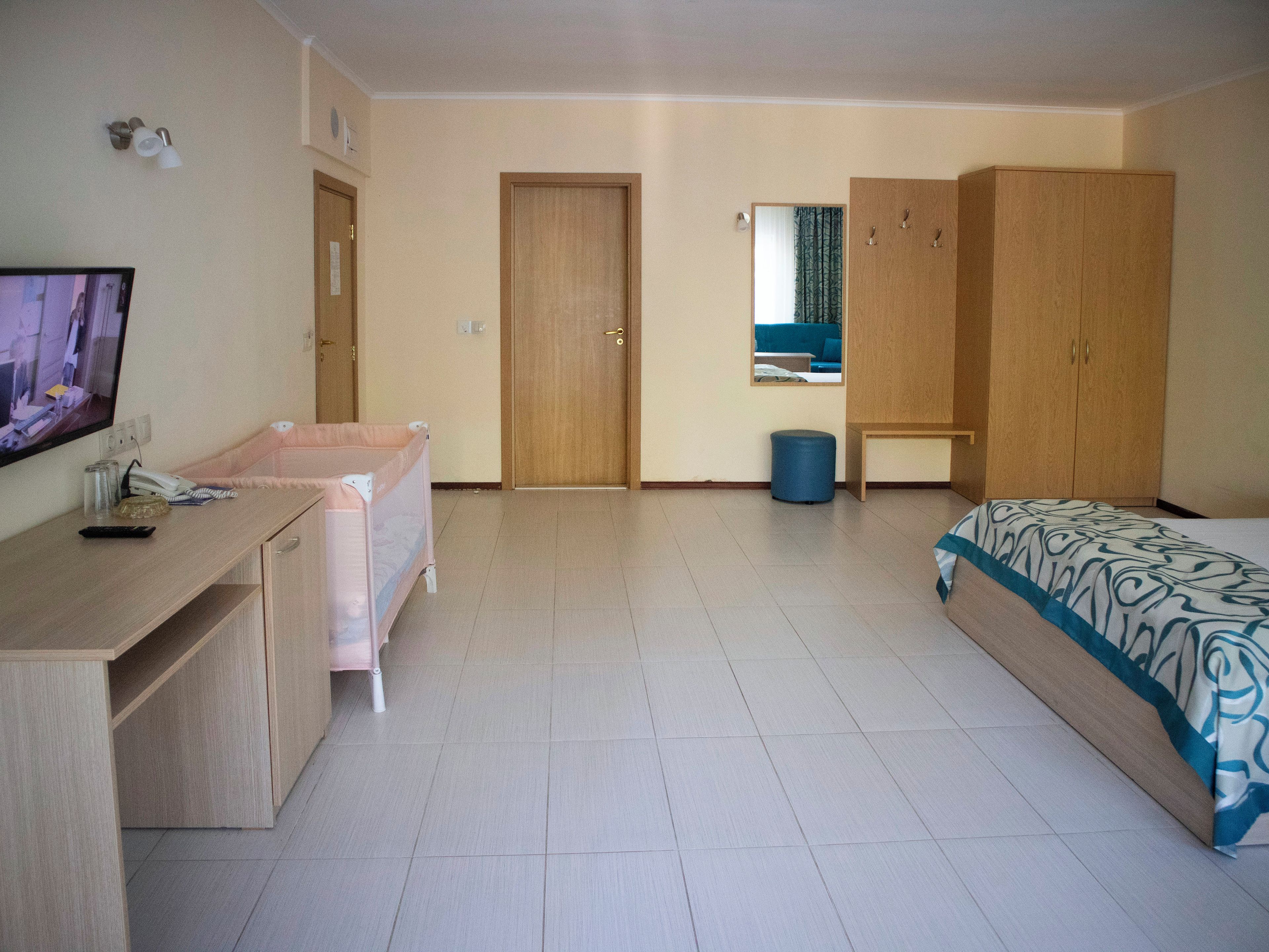 Quarto com cama, escrivaninha, cadeira, televisão e guarda-roupa.