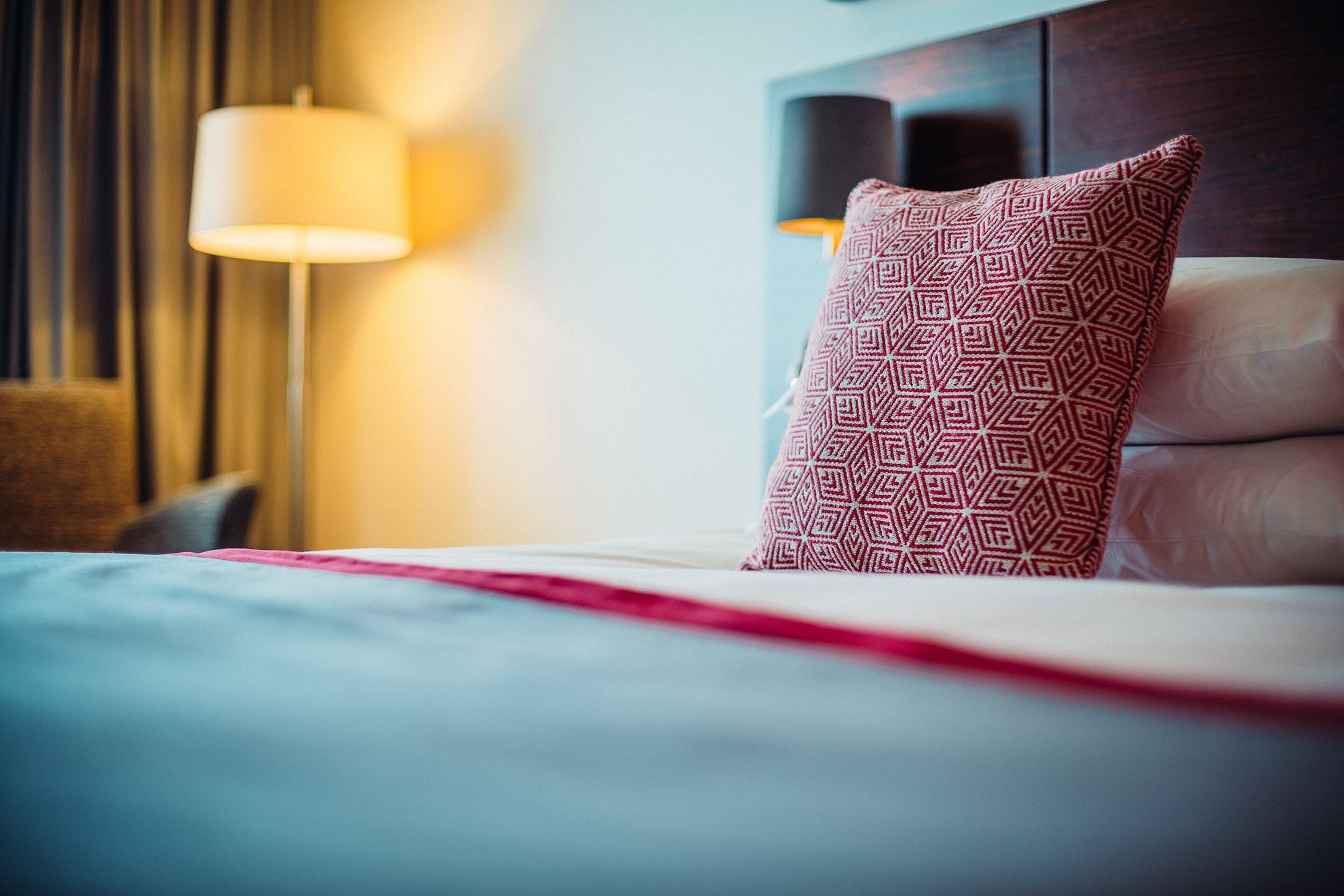 Cama bem arrumada com travesseiro estampado, abajur e cabeceira de madeira.