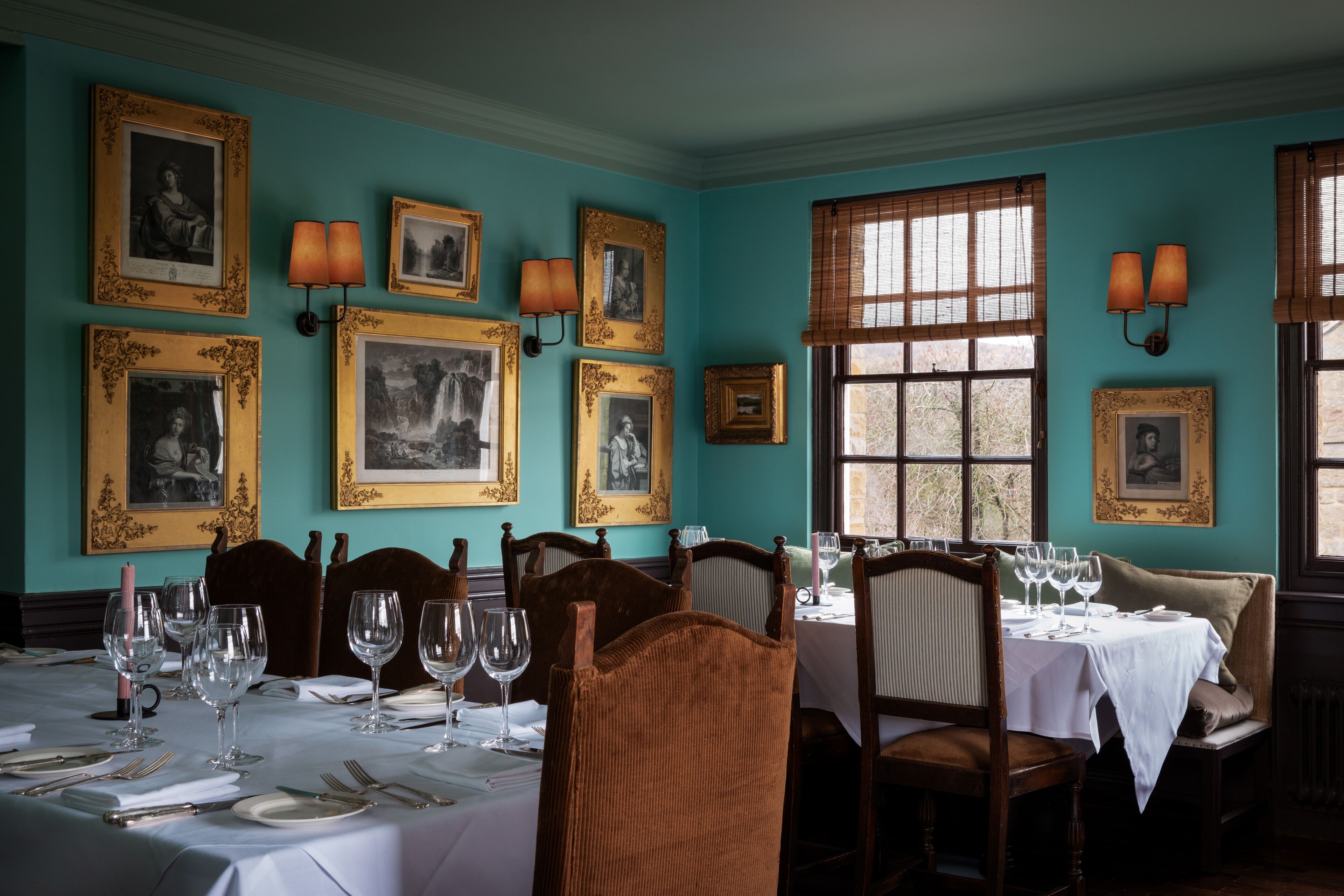 Uma sala de jantar com paredes verde-água, quadros enquadrados e uma mesa posta para refeição.