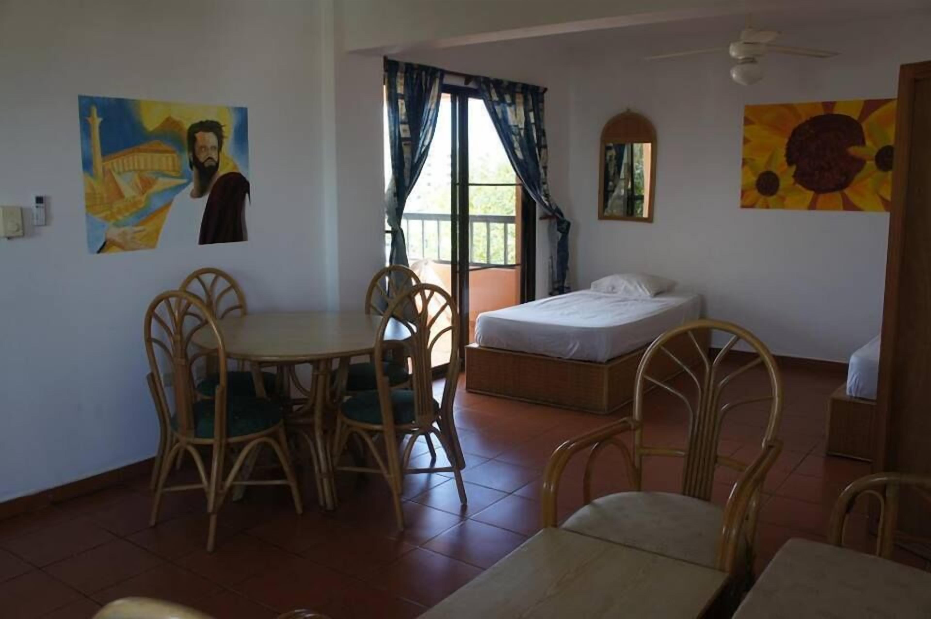 Quarto com uma cama, uma mesa de jantar com cadeiras e duas pinturas nas paredes.