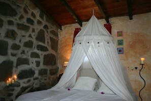 Quarto com paredes de pedra e cama sob um dossel branco.