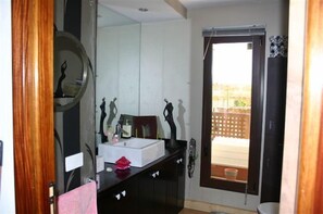 Casa de banho com lavatório branco, armários escuros, um espelho grande e vista para um deck de madeira através de uma porta de vidro.