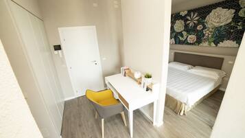 Quarto compacto com cama, escrivaninha e cadeira, e uma porta.