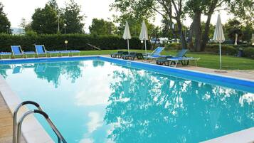 Piscina retangular com superfície de água azul cristalina, rodeada por espreguiçadeiras e guarda-sóis.