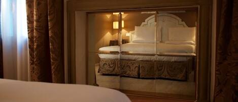 Quarto de hotel com uma cama grande, um guarda-roupa espelhado e uma mesa de cabeceira com abajur.