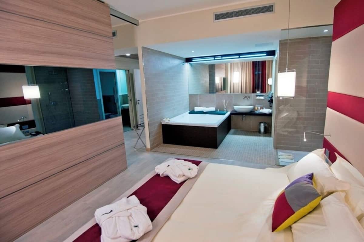 Quarto de hotel moderno com uma cama grande, banheiro separado e área de estar com toalhas.