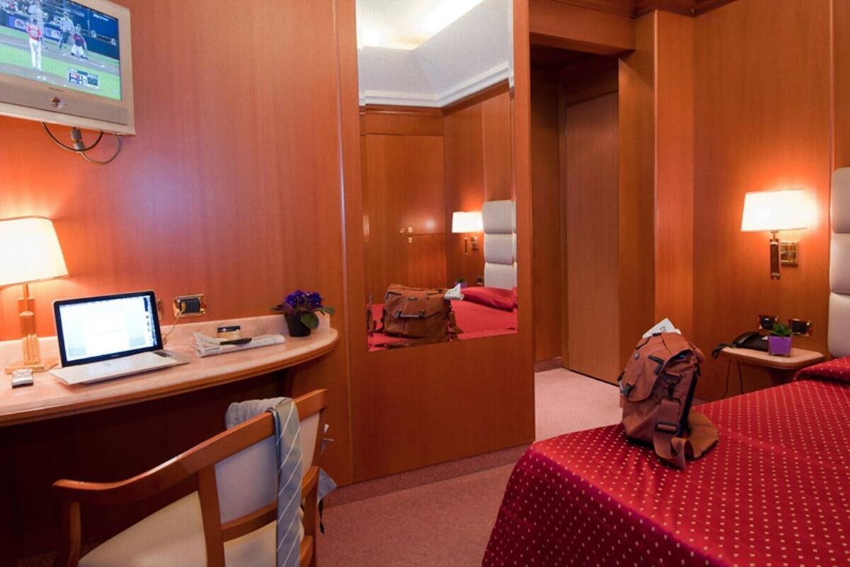 Quarto de hotel com escrivaninha, laptop, duas camas, televisão e mesa de cabeceira com abajur.
