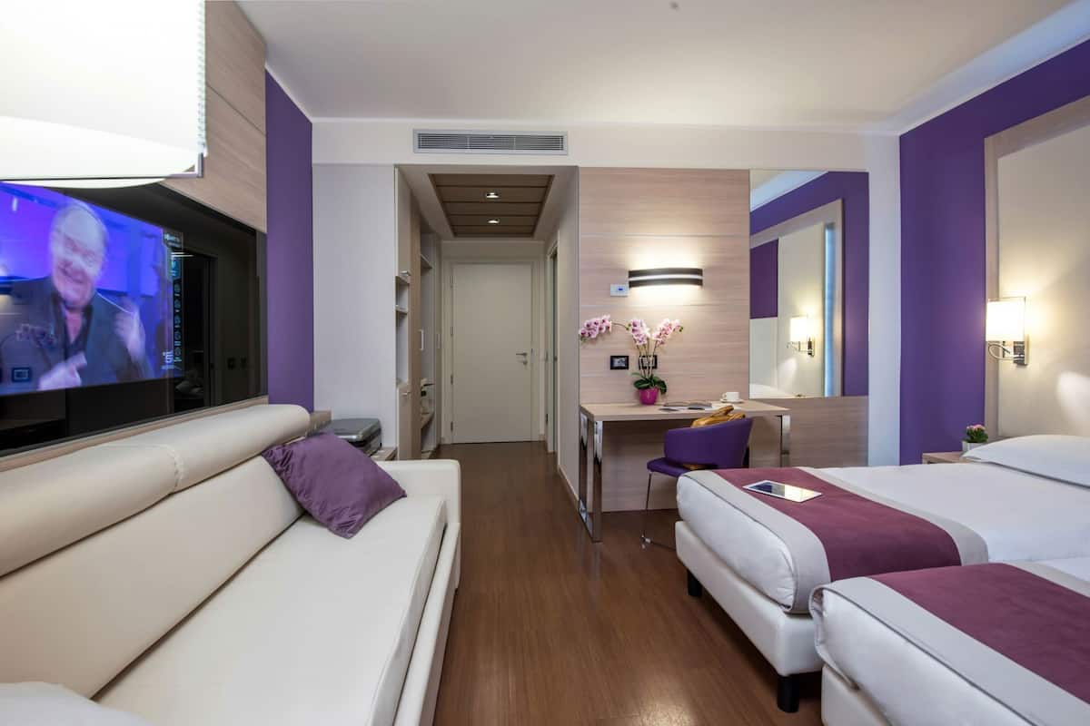 Quarto de hotel com televisão, escrivaninha, cadeira, cama e espelho.