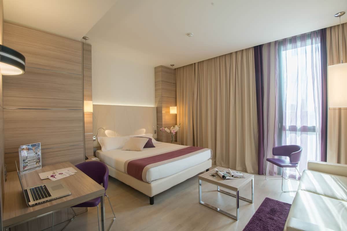 Quarto de hotel moderno com cama, escrivaninha e área de estar.