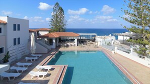 Área de piscina com espreguiçadeiras e vista para o mar.