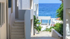 Escadaria que leva a uma varanda com vista para o mar, onde se pode ver um edifício com fachada branca e telhado de telhas vermelhas.