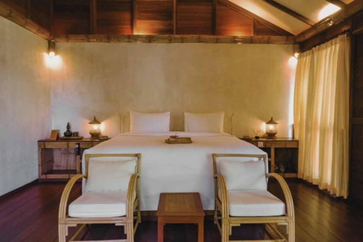 Um quarto com uma cama grande, duas mesas de cabeceira com luminárias e duas cadeiras de vime.