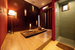 Um espaço de spa com piso de madeira, uma mesa de massagem, uma lâmpada de massagem fixada na parede, uma janela com cortinas e um ar condicionado.