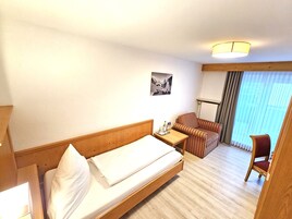 Quarto de hotel com cama de madeira, sofá listrado, uma pequena mesa com luminária e uma cadeira.