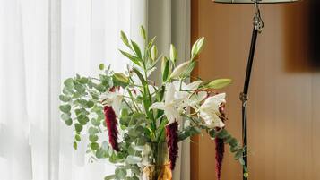 Uma mesa de madeira com um vaso de flores e limões, uma lâmpada e uma janela com cortinas leves.