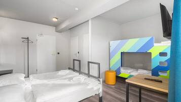 Quarto de hotel com duas camas, uma escrivaninha, uma televisão e uma parede colorida.