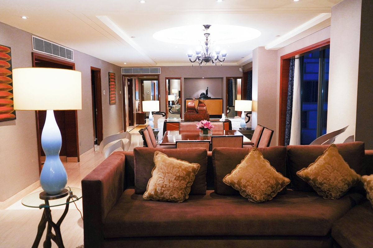 Um saguão de hotel moderno com sofá, luminárias, um candelabro e uma área de refeições.
